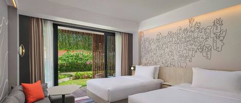 Quarto de hotel com duas camas, um sofá, uma mesinha e vista para um jardim através de grandes janelas.