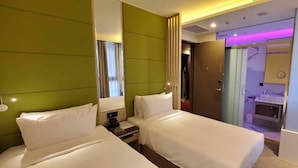 Quarto de hotel com duas camas, uma mesa de cabeceira, um espelho e um banheiro visível através de uma porta aberta.