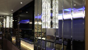 Um hall de hotel moderno com divisórias de vidro refletivo, balcão de recepção e iluminação ambiente.