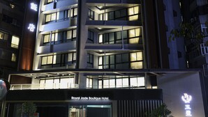Um hotel de vários andares com janelas iluminadas e uma placa com a inscrição 'Royal Jade Boutique Hotel'.