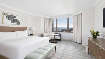 Quarto de hotel com uma cama grande, área de estar, escrivaninha e vista da cidade.