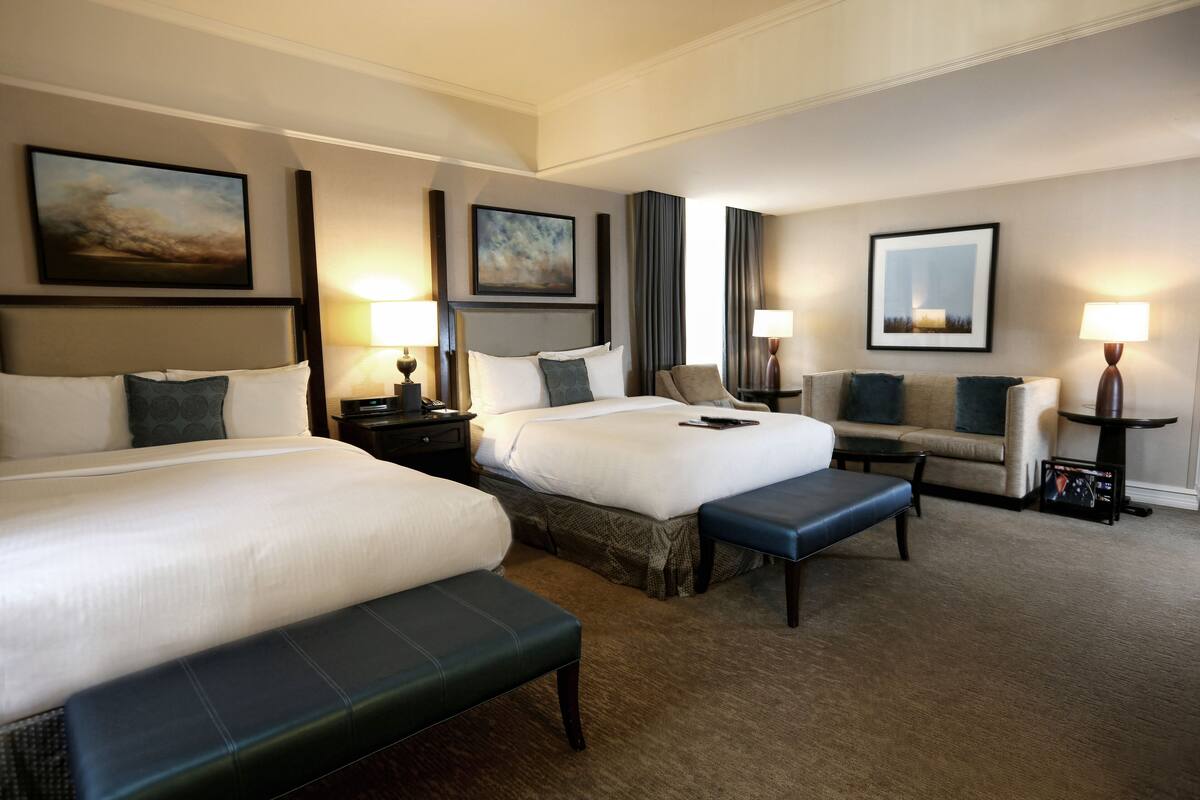 Quarto de hotel com duas camas, um sofá, uma mesa de centro e uma televisão.
