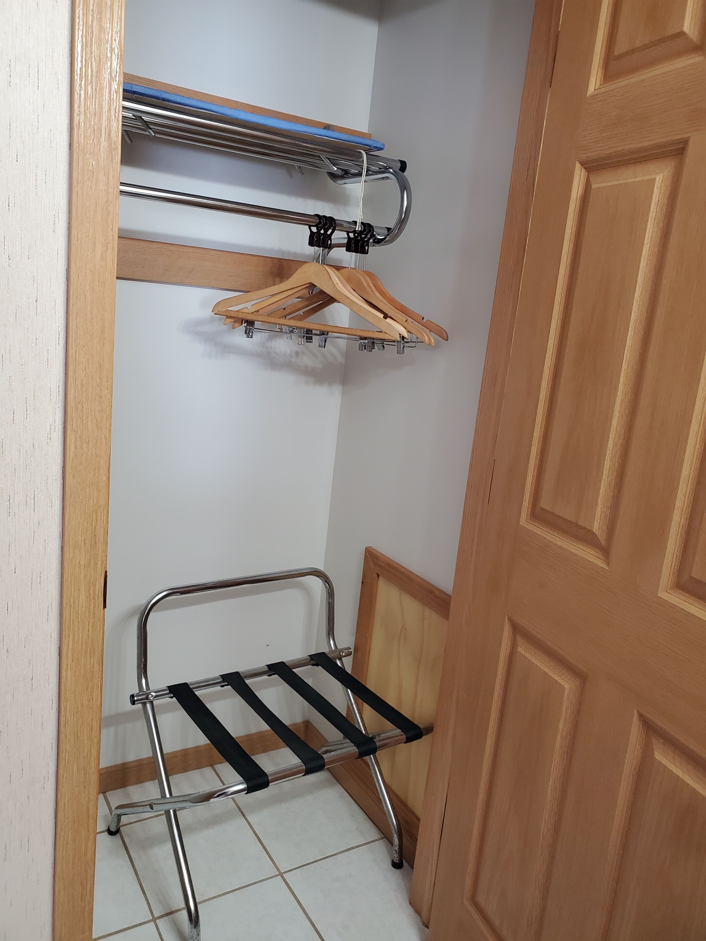 Canto de um quarto com uma porta de madeira, um varal de metal e uma estante de madeira com cabides.