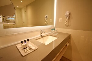 Uma casa de banho moderna com um espelho grande, uma pia e dois secadores de cabelo fixados na parede.