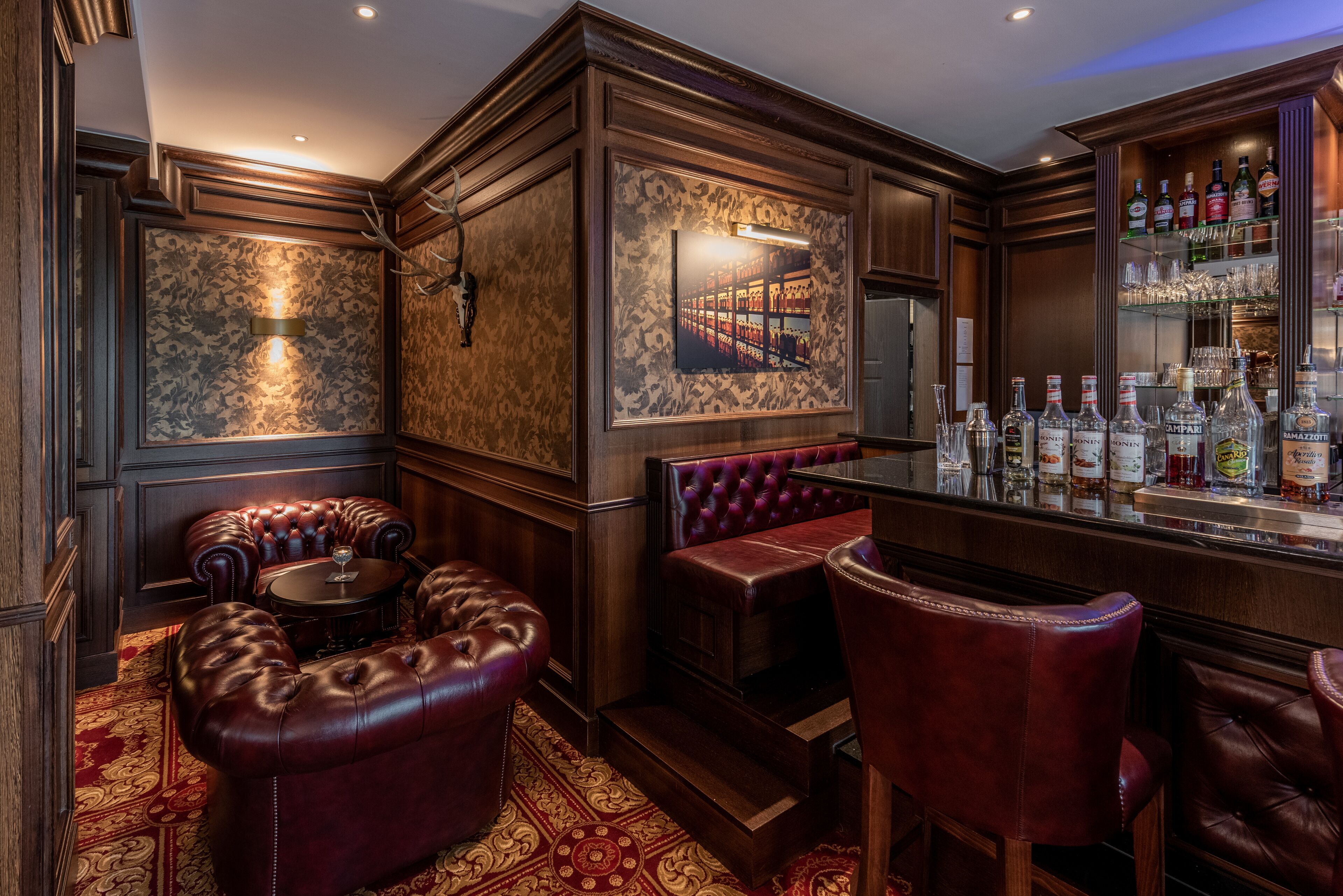 Uma área de bar com assentos de couro, balcão e prateleiras com bebidas.