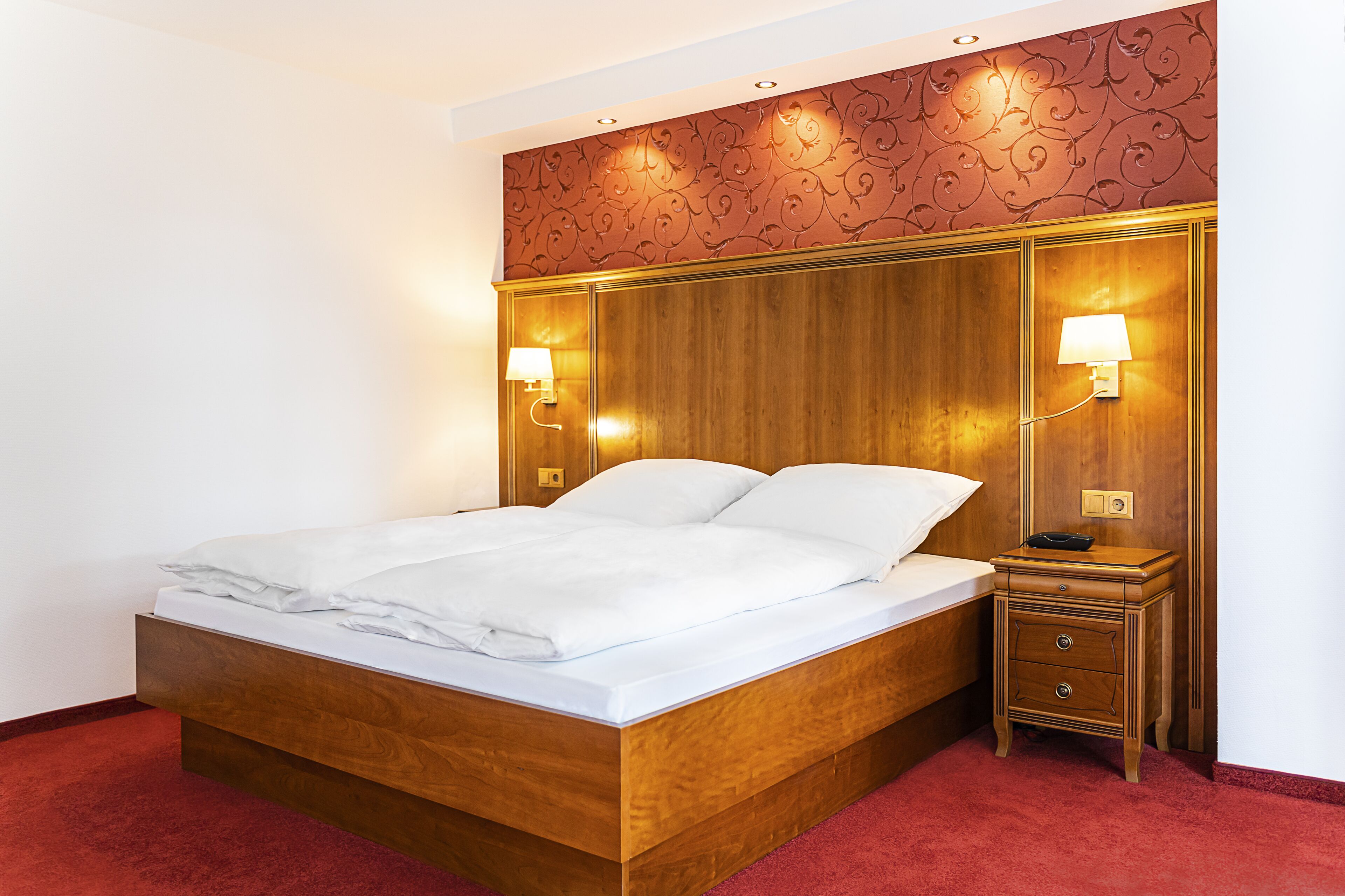 Cama bem arrumada com cabeceira de madeira e duas luminárias de cabeceira.