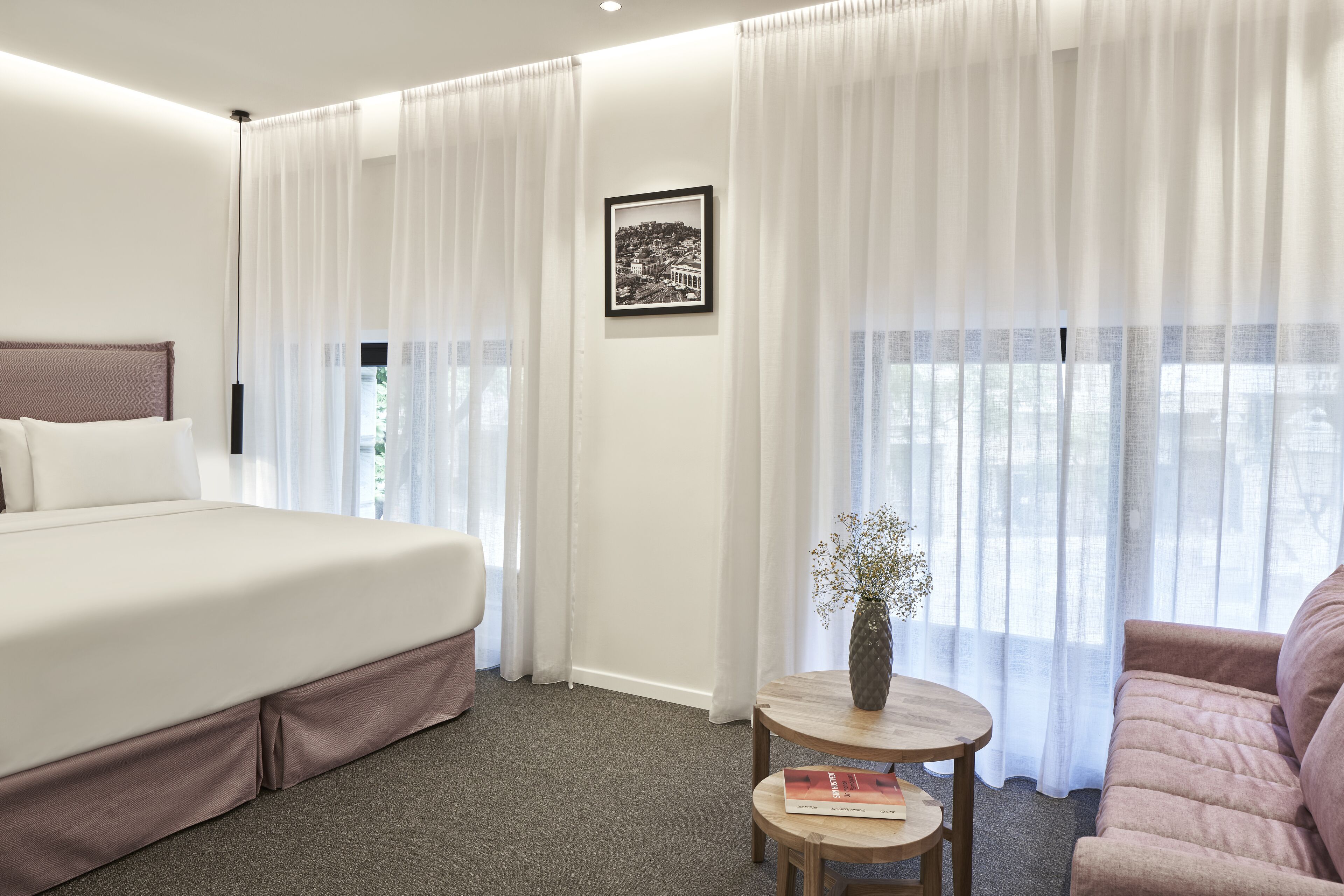 Quarto de hotel com uma cama grande, uma mesinha com um vaso e um sofá.