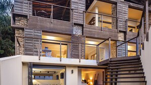Uma casa moderna de dois andares com escada de madeira, paredes de pedra e varanda.