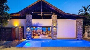 Uma casa moderna com piscina, pilares de pedra e interior bem iluminado.