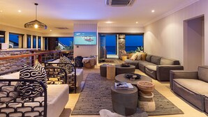 Uma sala de estar moderna com uma televisão grande, assentos confortáveis e vista para o oceano.