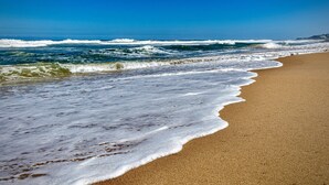 Uma praia com ondas quebrando na costa sob um céu azul claro.