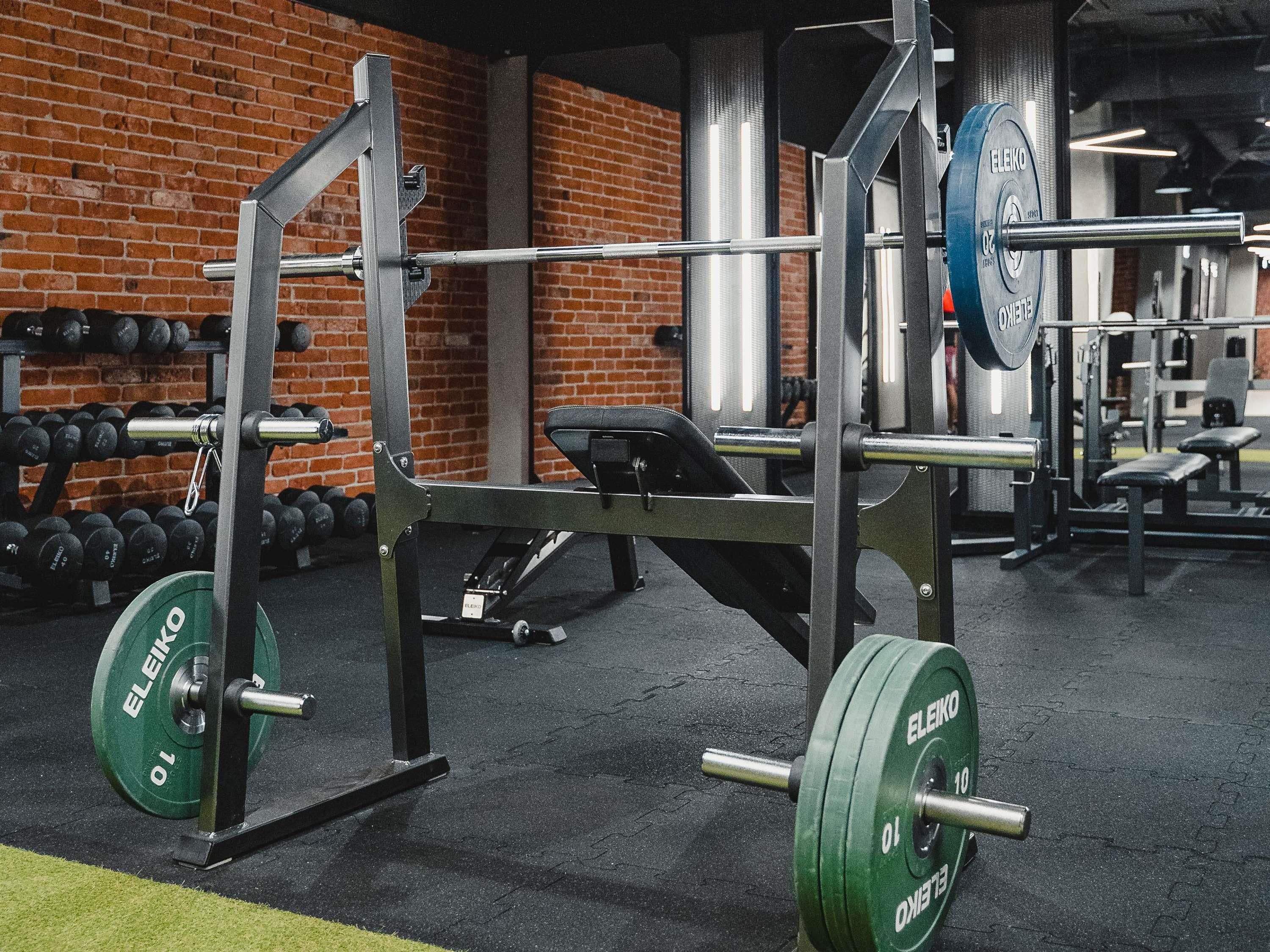 Uma academia com equipamentos de musculação, incluindo um suporte para agachamento e barra.