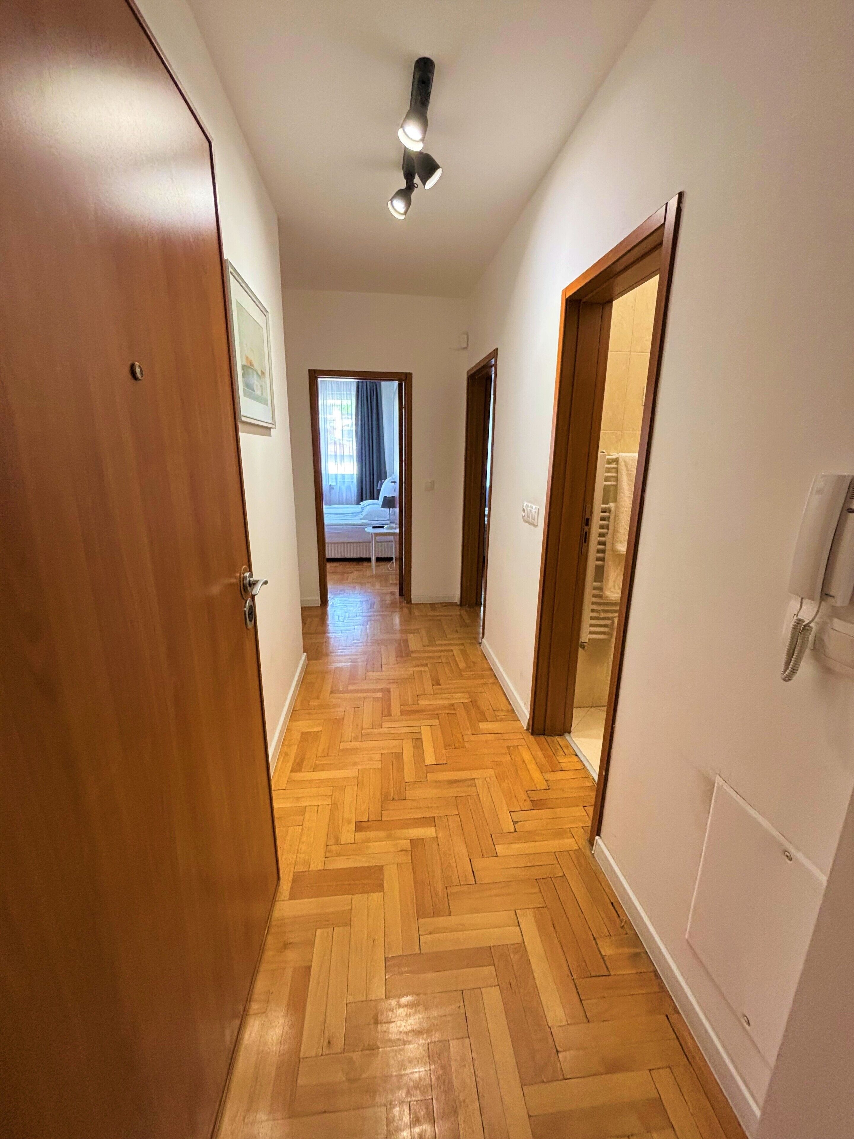 Um corredor com piso de madeira, ventilador de teto e portas que dão para quartos.