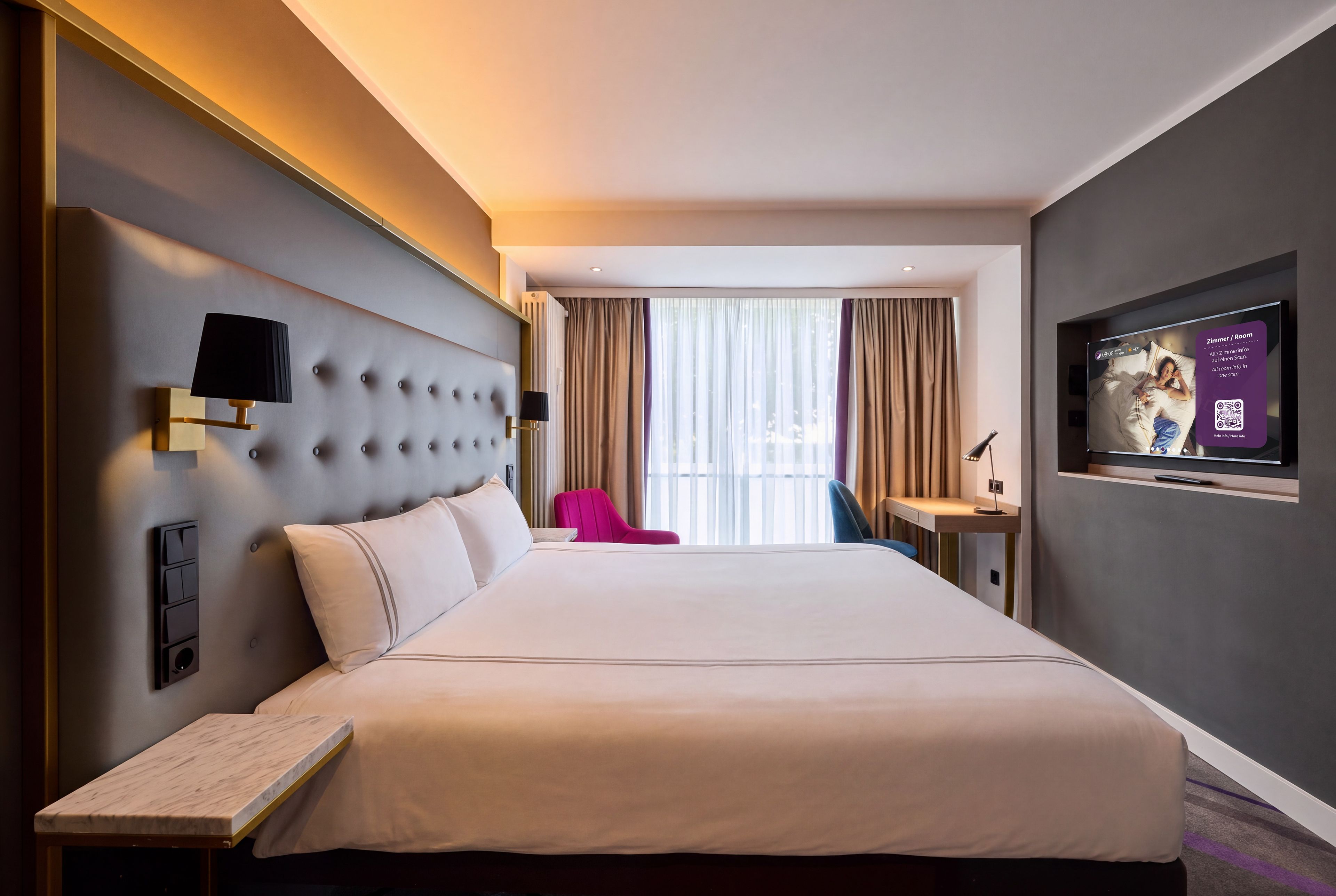 Quarto de hotel com uma cama grande, mesa de cabeceira, televisão e janela com cortinas.