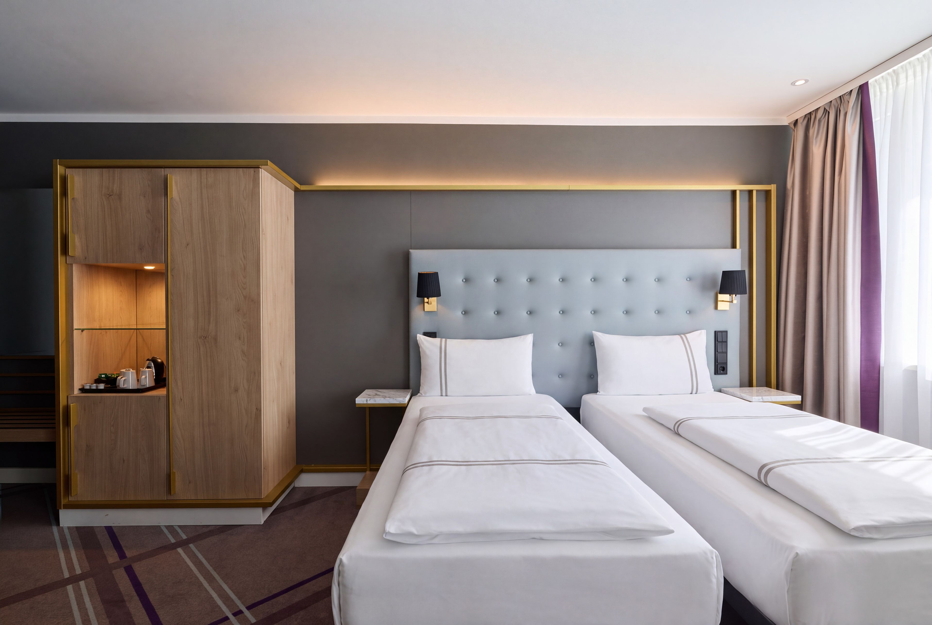 Quarto de hotel com duas camas, um guarda-roupa, uma mesa de cabeceira e uma luminária.