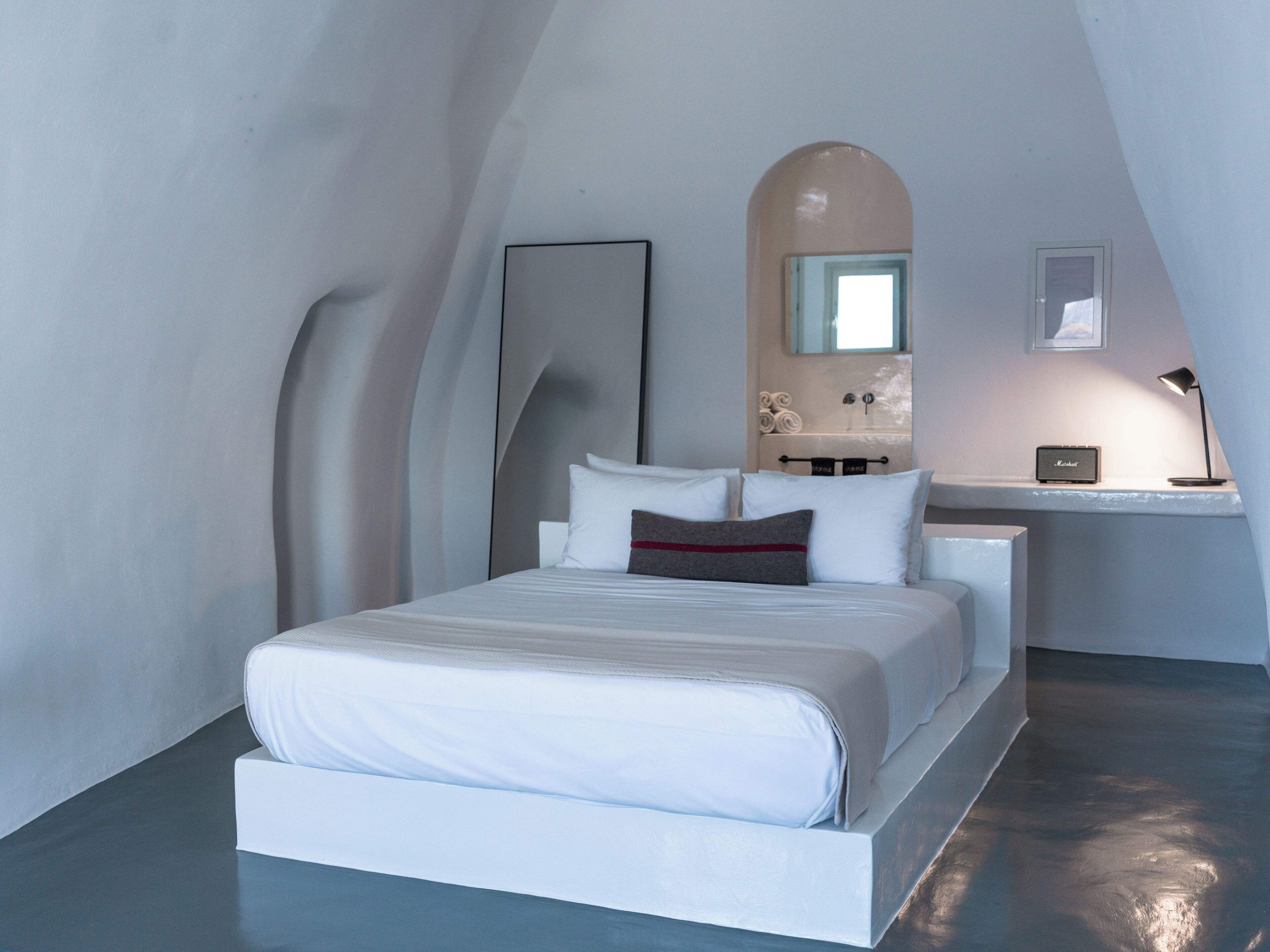 Quarto moderno com cama, mesa de cabeceira, abajur, espelho e vista do céu.