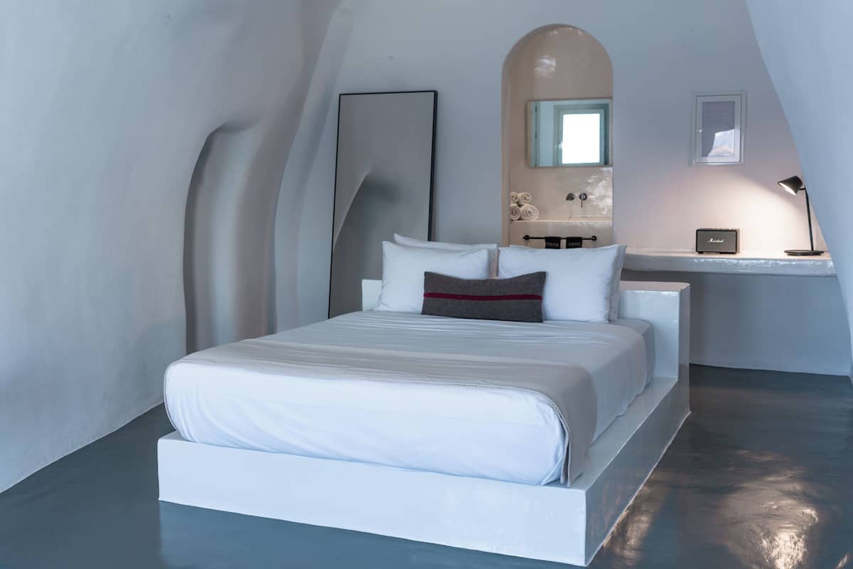Quarto moderno com cama, mesa de cabeceira, abajur, espelho e vista do céu.
