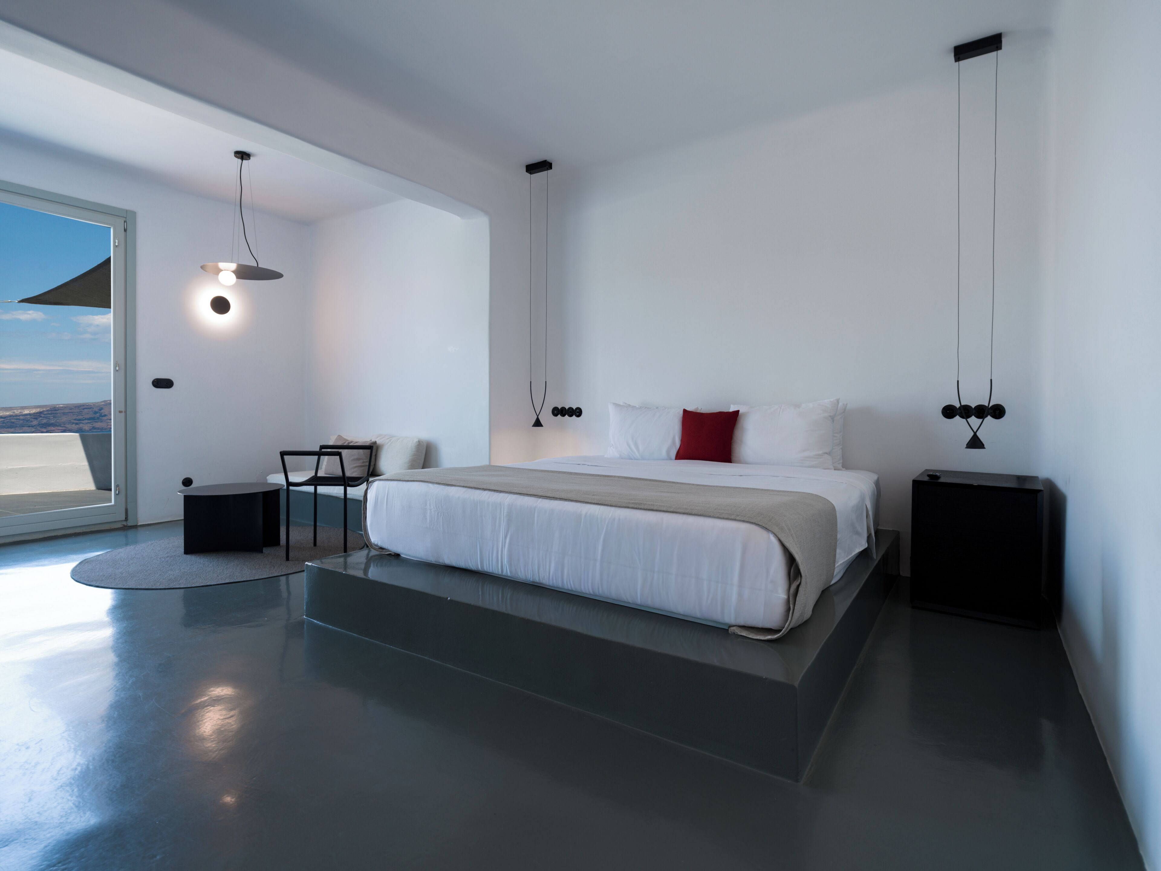 Quarto moderno com uma cama grande, mesas de cabeceira, uma cadeira e vista pela janela.