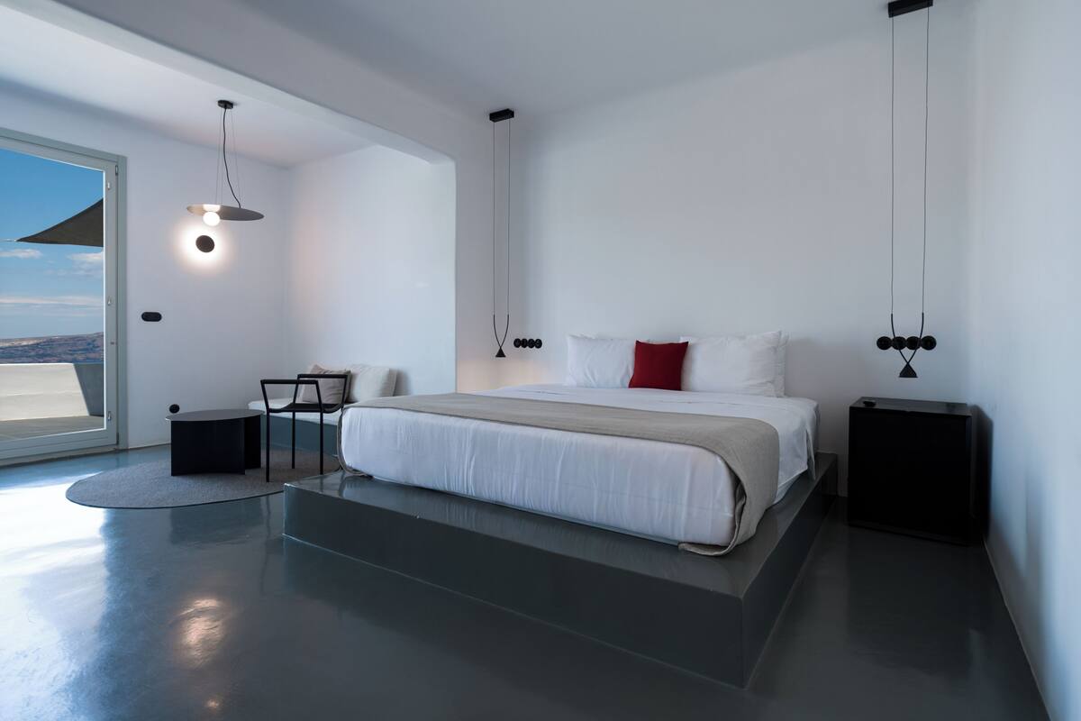 Quarto moderno com uma cama grande, mesas de cabeceira, uma cadeira e vista pela janela.