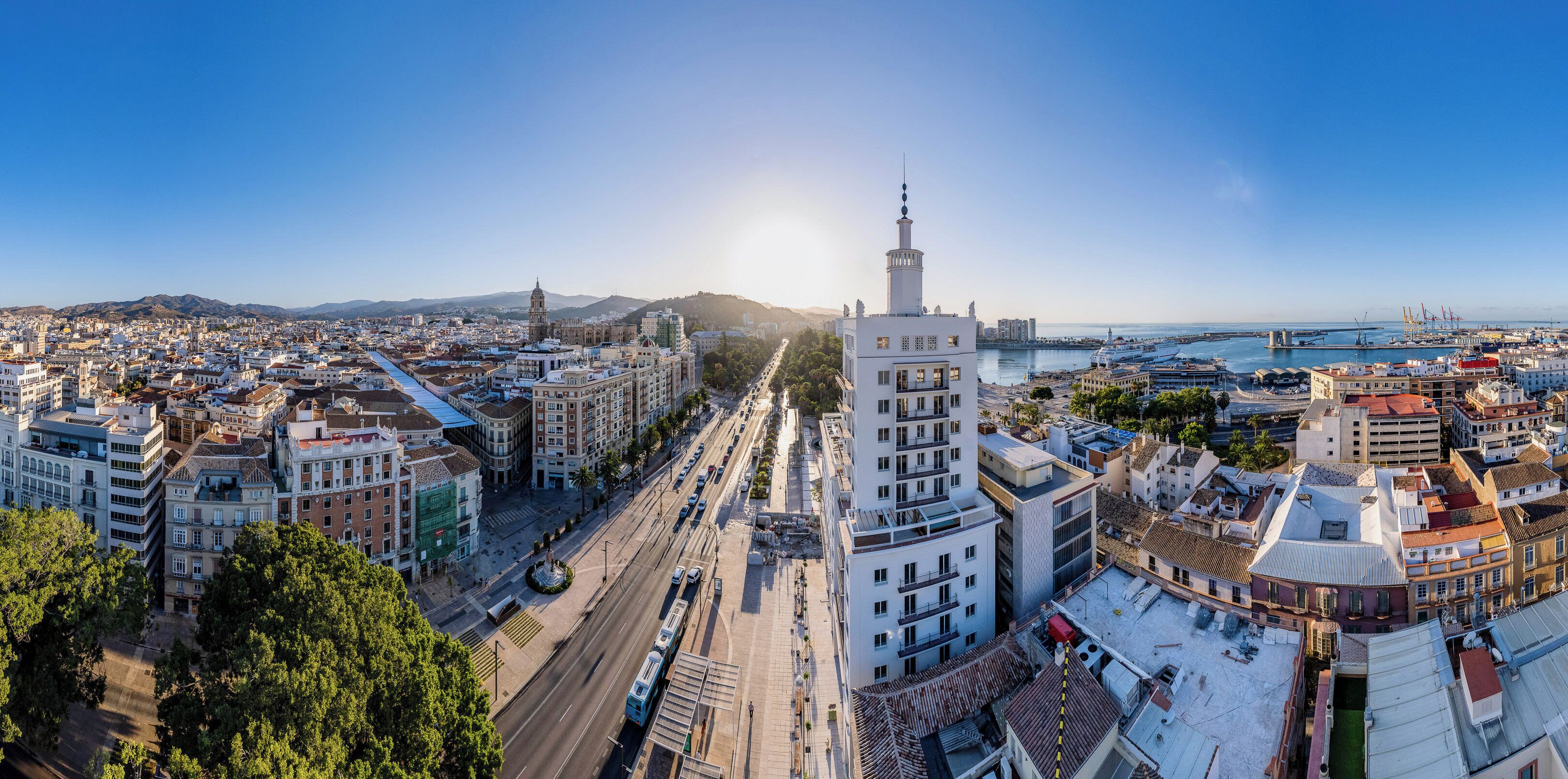 Paisagem urbana com uma torre branca imponente, uma rua movimentada e um porto com guindastes.