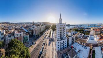 Paisagem urbana com uma torre branca imponente, uma rua movimentada e um porto com guindastes.