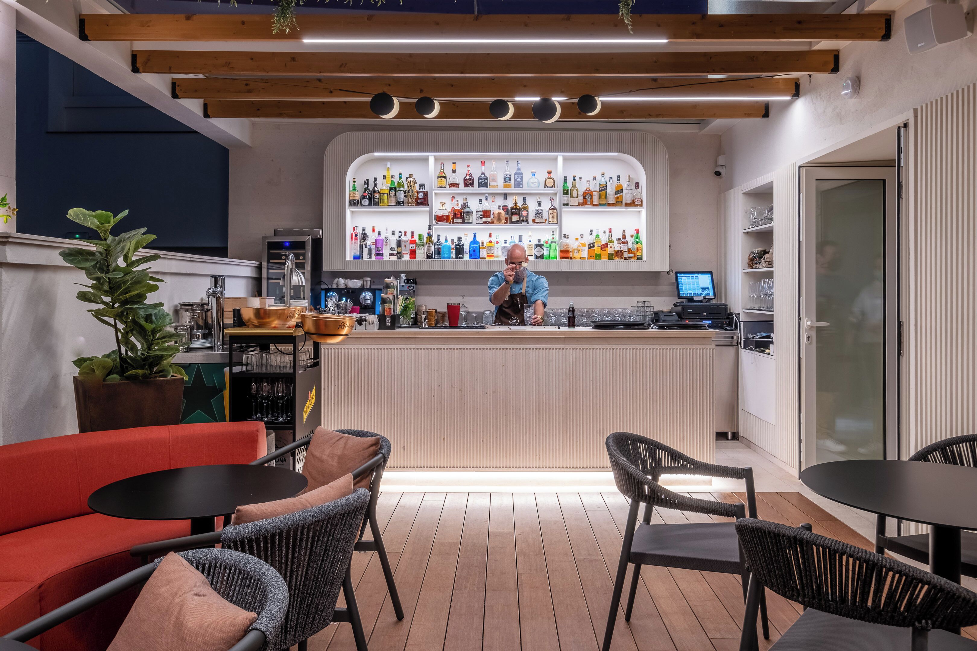 Uma área de bar com balcão, prateleiras cheias de garrafas e assentos com cadeiras e um sofá.