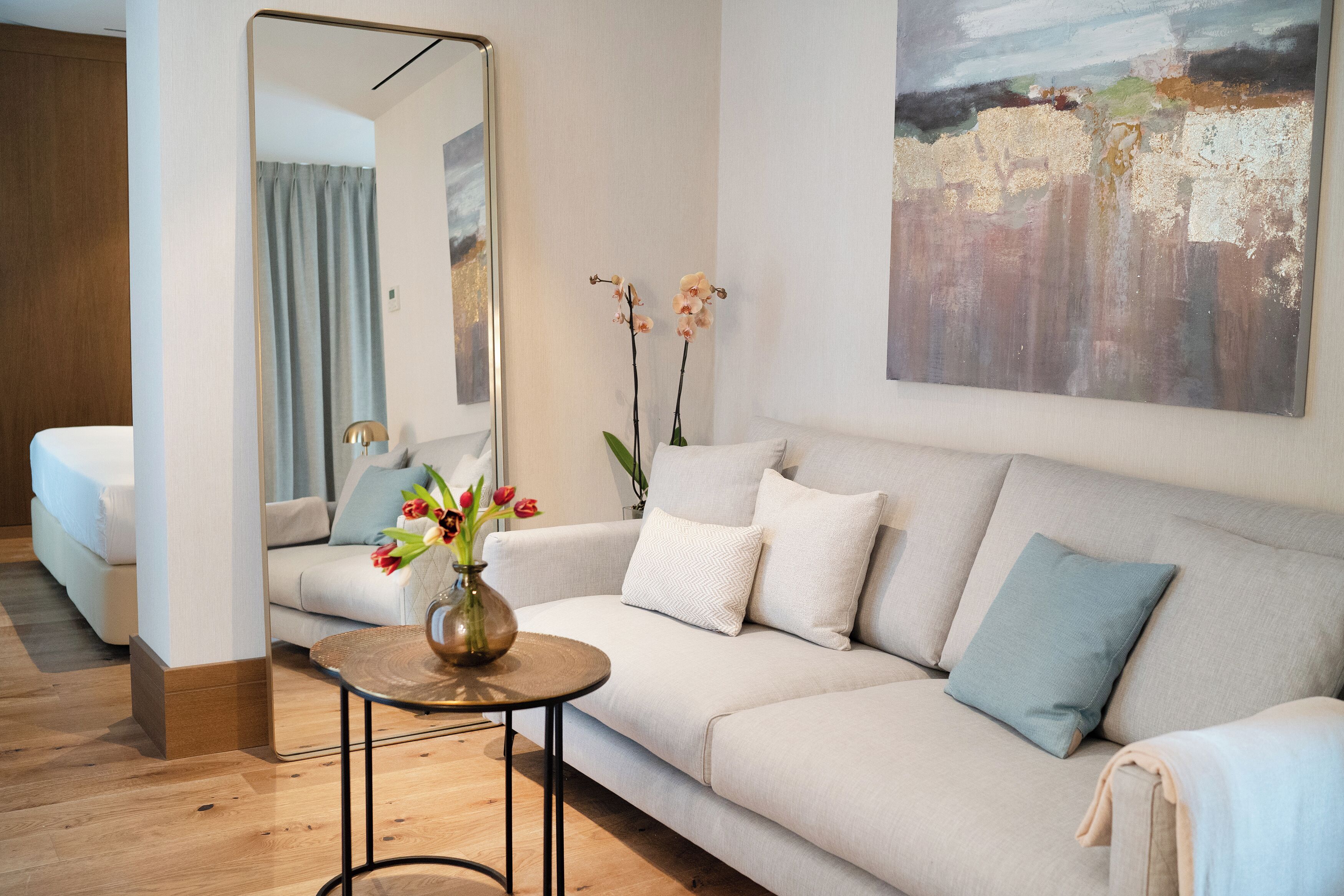 Uma sala de estar moderna com um sofá, uma mesa de centro, um vaso com flores, um espelho grande e um quadro na parede.