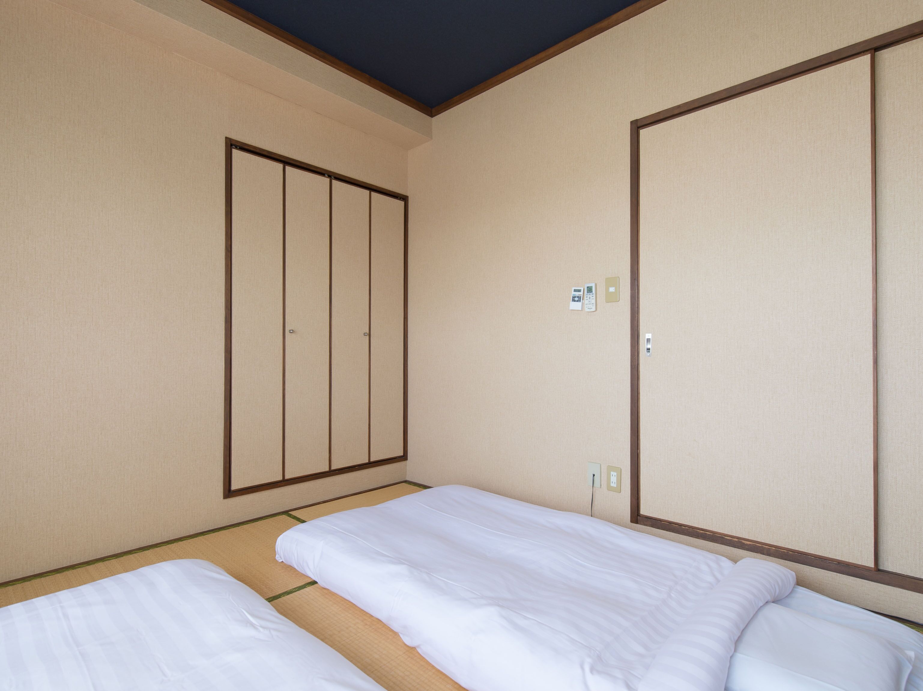 Quarto de hotel com duas camas, um guarda-roupa espaçoso e teto com vigas de madeira.