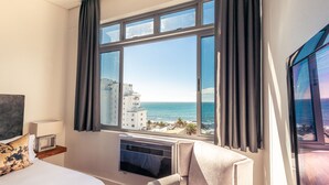 Quarto de hotel com uma grande janela que oferece vista para o oceano e prédios.