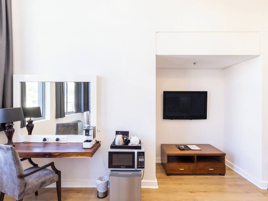 Quarto de hotel moderno com escrivaninha de madeira, uma cadeira, micro-ondas, televisão e um cesto de lixo pequeno.