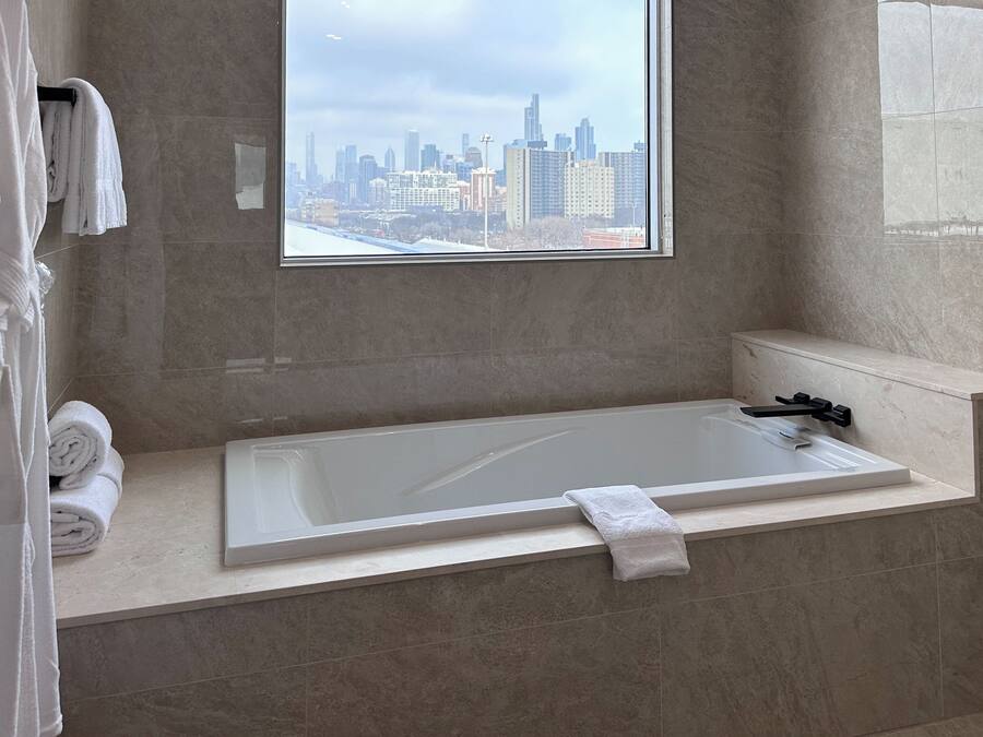Um banheiro moderno com uma banheira grande, uma janela com vista para a cidade e toalhas dobradas em uma prateleira.