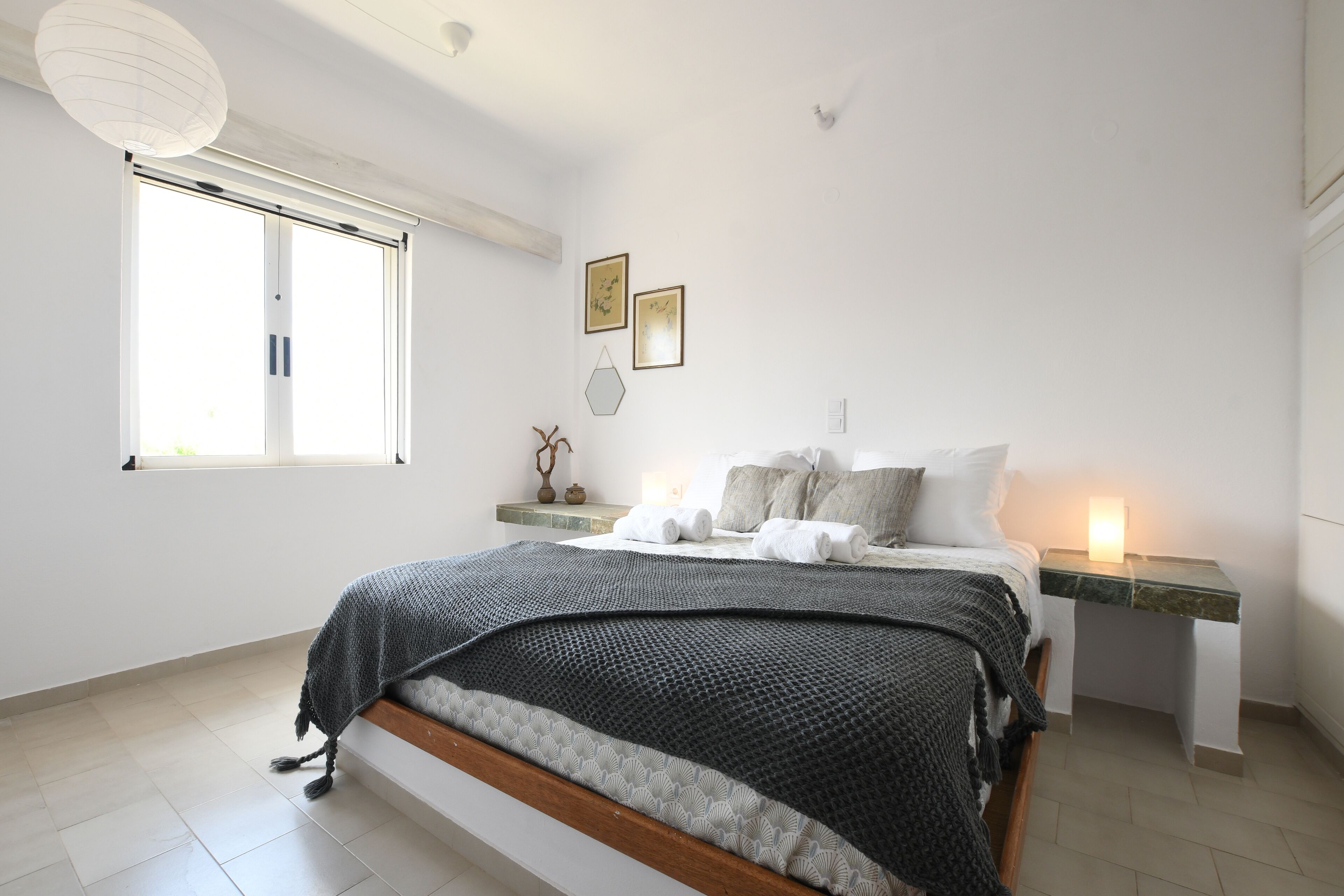 Quarto com cama, mesas de cabeceira, janela e decorações nas paredes.