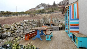Um deck de madeira com área de estar ao ar livre, um muro de pedra e um edifício colorido ao fundo.