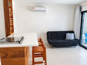 Um espaço de estar moderno com cozinha branca, sofá preto e mesa de jantar com tampo de vidro.