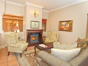 Uma sala de estar com lareira, dois poltronas, um sofá, uma mesa de centro e um candelabro.