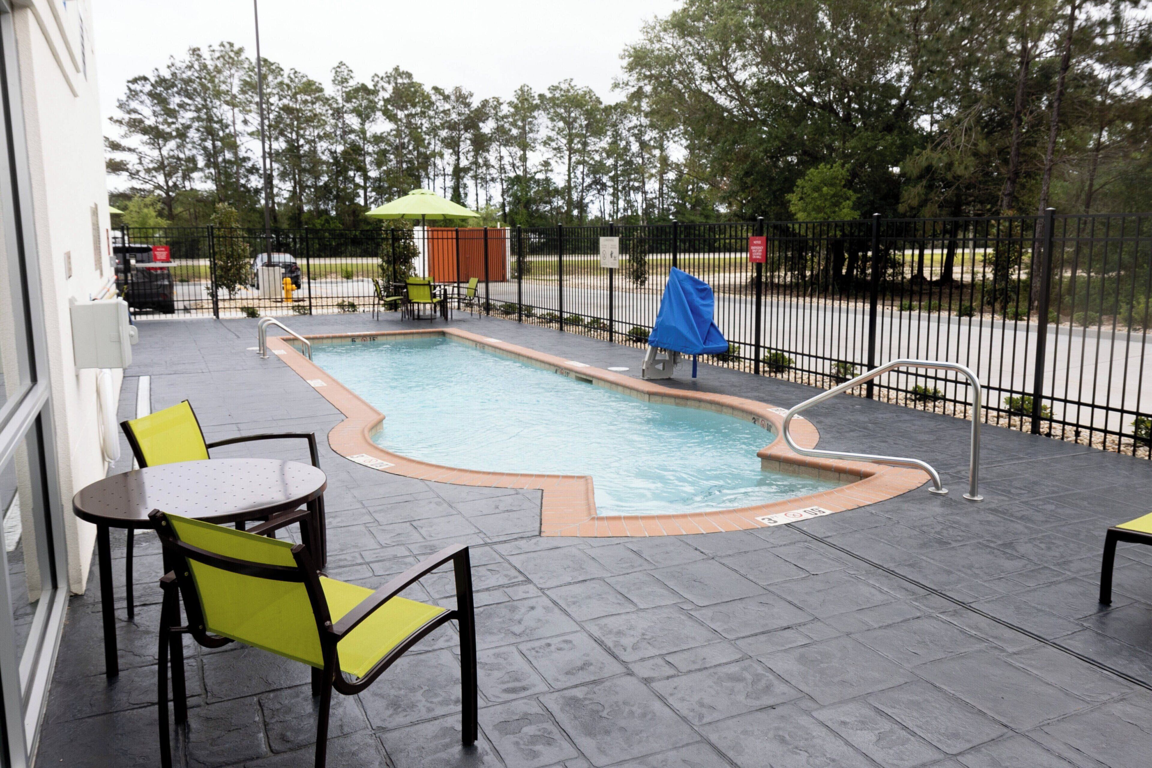 Uma piscina com deck revestido, rodeada por uma cerca e uma área de estar coberta com cadeiras.