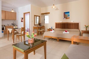 Quarto de hotel com cama, mesa de cabeceira, pequena escrivaninha com cadeira, mesa de jantar com cadeiras, cozinha e banheiro.