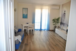 Uma sala de estar com sofá, mesa de jantar, cadeiras e televisão.