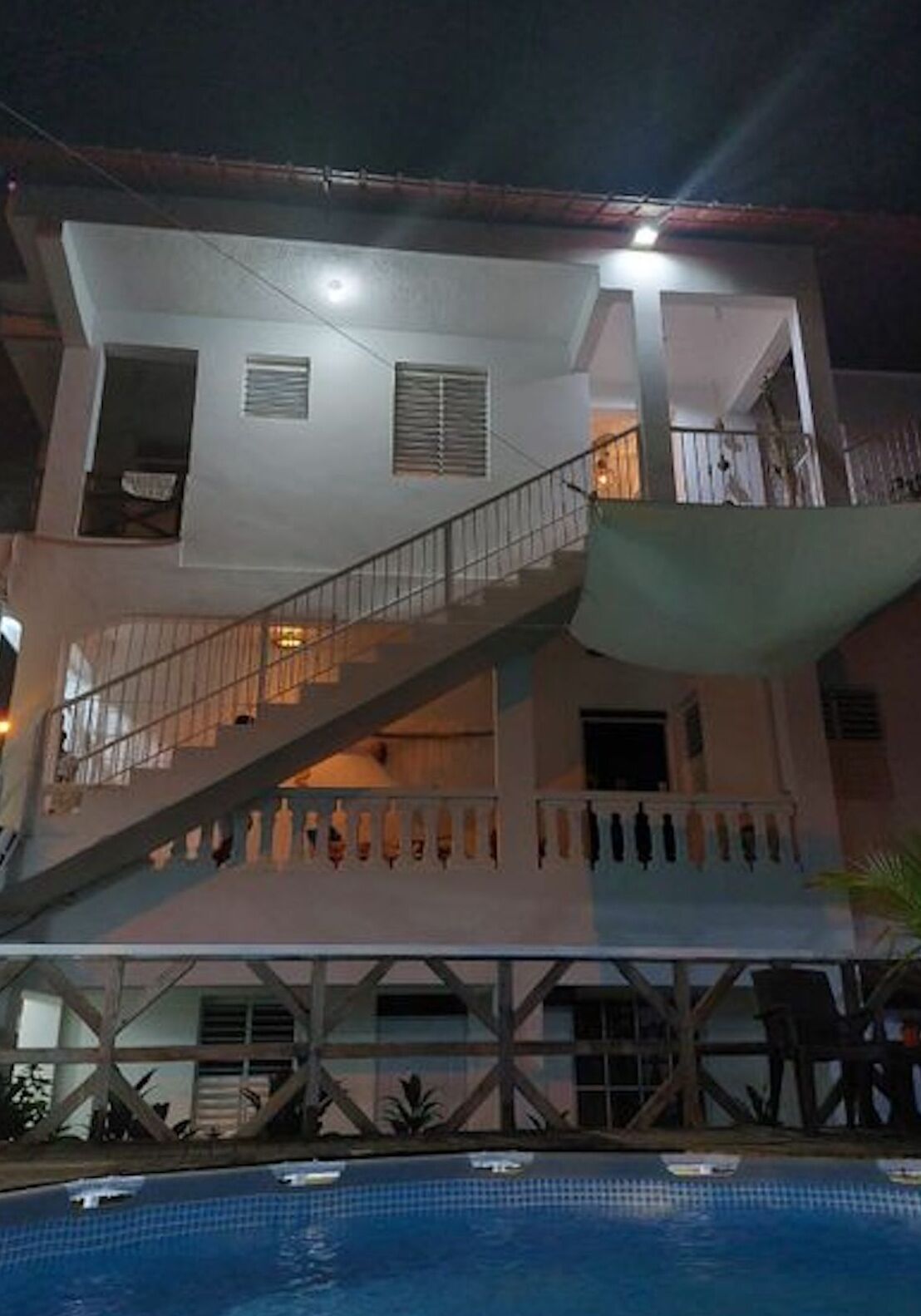 Um edifício de dois andares com uma varanda no andar superior, uma escadaria que leva à varanda e uma piscina em primeiro plano.