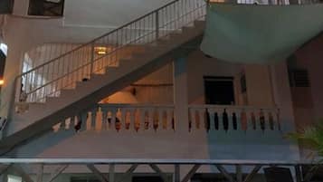 Um edifício de dois andares com uma varanda no andar superior, uma escadaria que leva à varanda e uma piscina em primeiro plano.