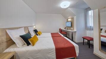 Quarto de hotel com duas camas, uma escrivaninha, uma cadeira, uma televisão e um espelho.