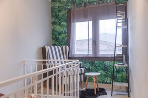 Quarto com berço, cadeira listrada, mesa pequena, escada e janela com cortina.