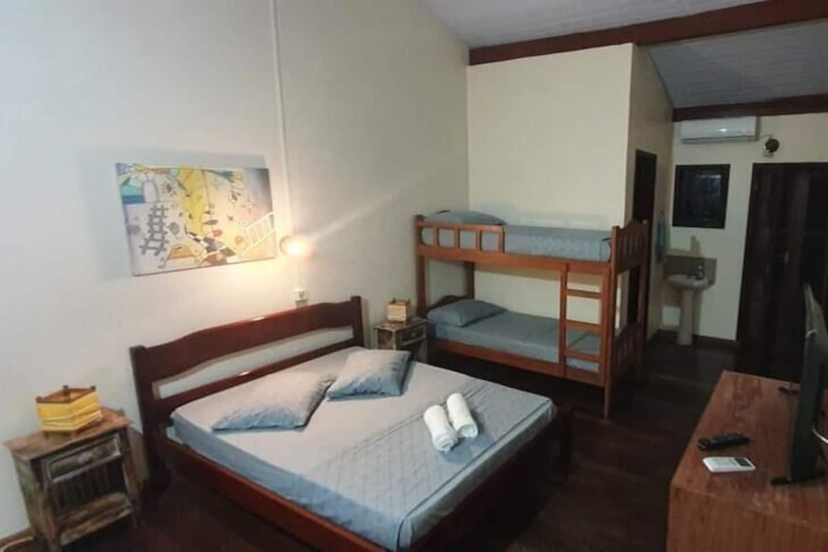 Quarto com uma cama de solteiro, uma cama beliche, uma escrivaninha e uma televisão.