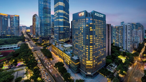 Um edifício alto com uma placa chamativa "ASCOTT", rodeado por outros arranha-céus modernos e uma rua urbana movimentada.