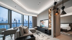 Uma sala de estar moderna com uma televisão grande, um sofá, um espaço de refeições e vista para a paisagem urbana.