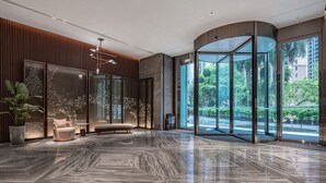 Um lobby moderno com entrada em vidro curvo, área de estar com um banco e uma planta em vaso.