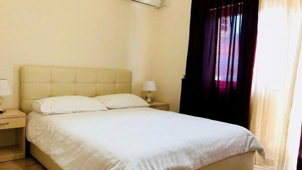 Quarto de hotel com uma cama grande, duas mesas de cabeceira, uma luminária e uma janela com cortinas.