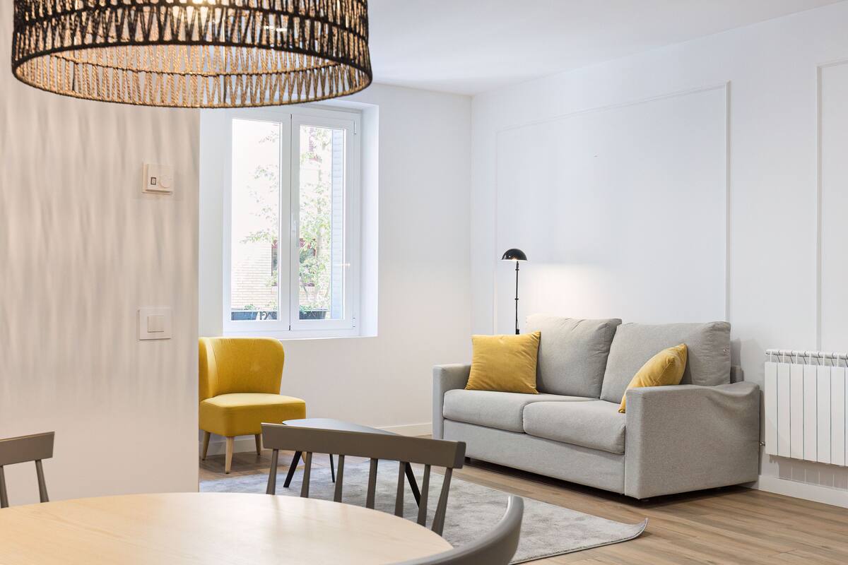 Uma sala de estar moderna com sofá, poltrona amarela e mesa de jantar.