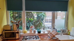 Cozinha equipada com fogão, micro-ondas e máquina de lavar louça. Tem uma janela com vista para o verde lá fora.