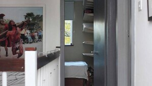 Um corredor estreito com teto branco, um radiador e uma cama ao fundo.